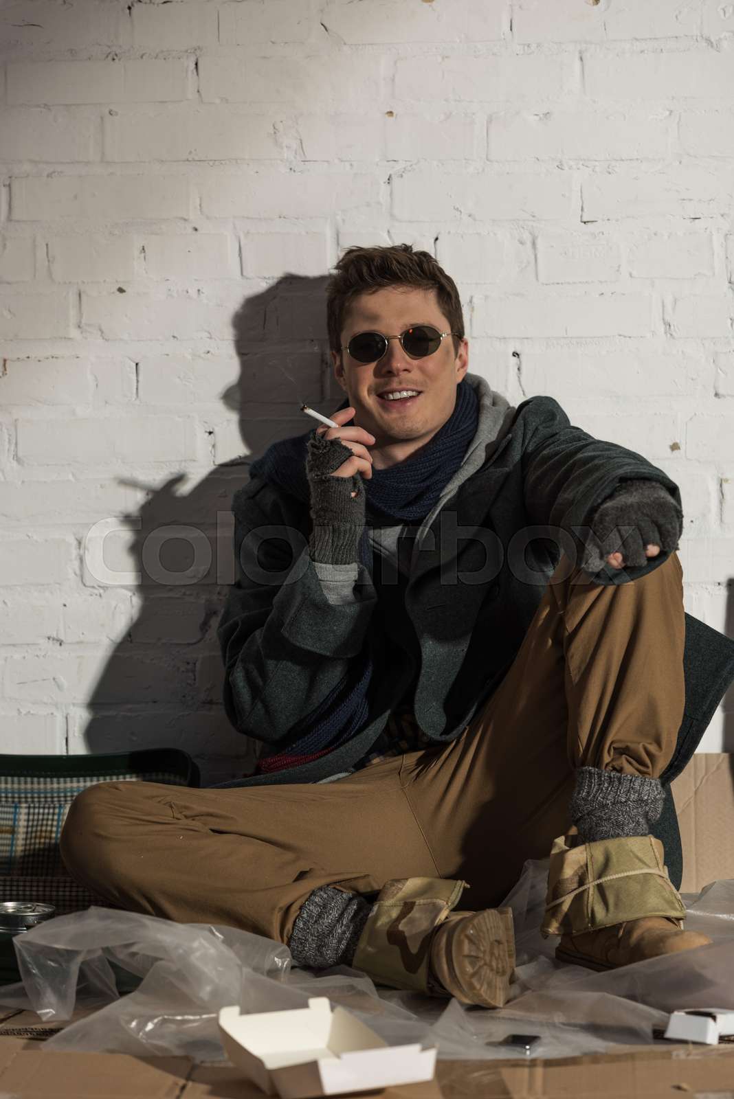 smiling homeless man smoking while sitting by brick wall | Stock image ...