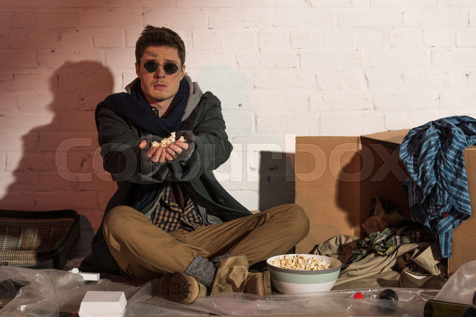 homeless man sitting by white brick wall and stretching hands with ...