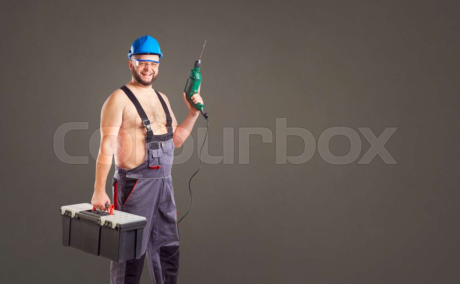 The fat funny man builder with a drill. | Stock image | Colourbox