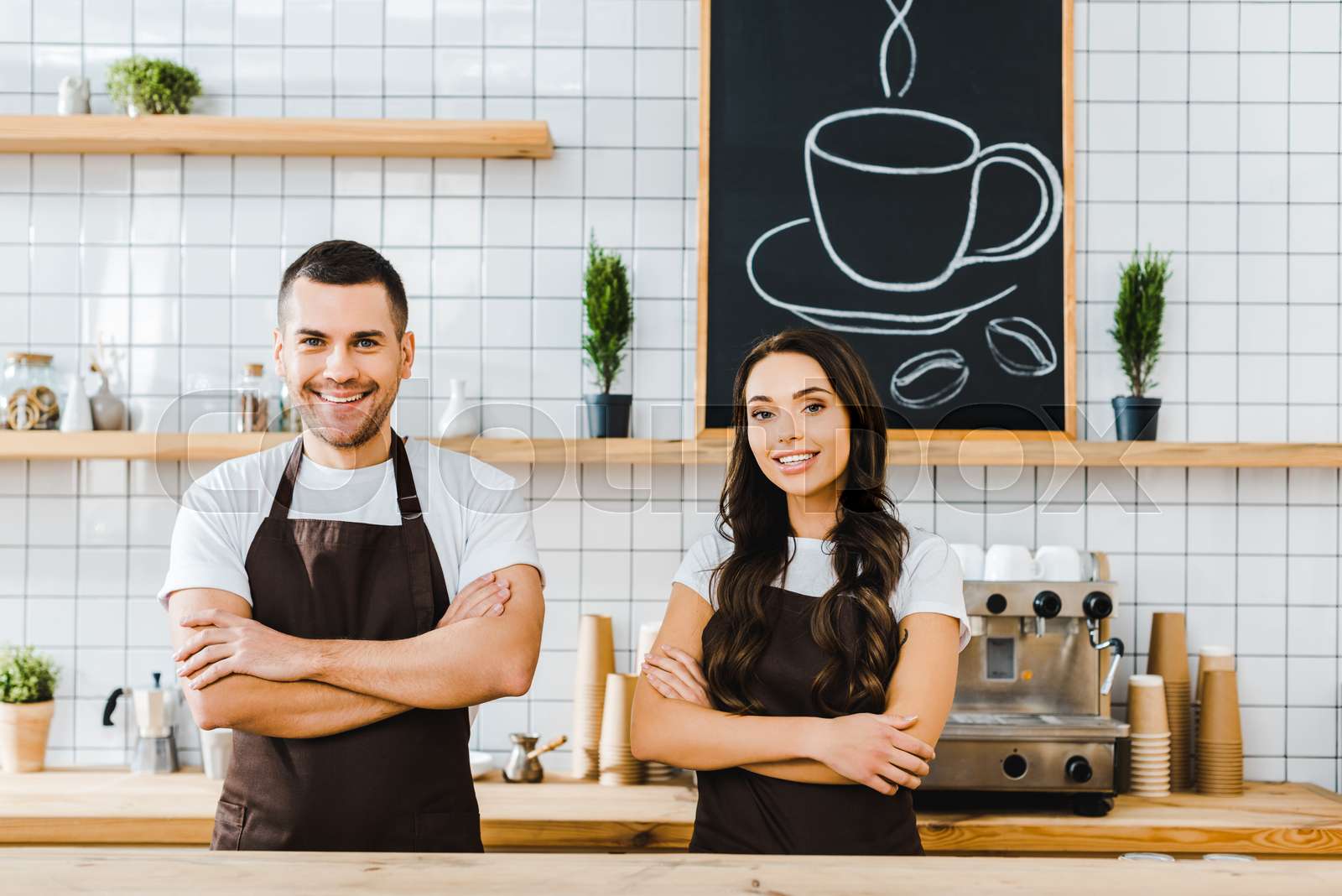 cashiers standing behind wooden bar counter and smiling in coffee house ...