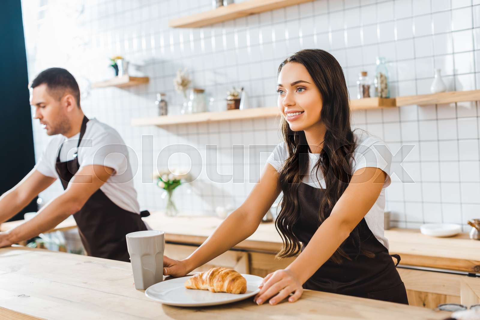 attractive cashier standing behind bar counter with cup, plate and ...