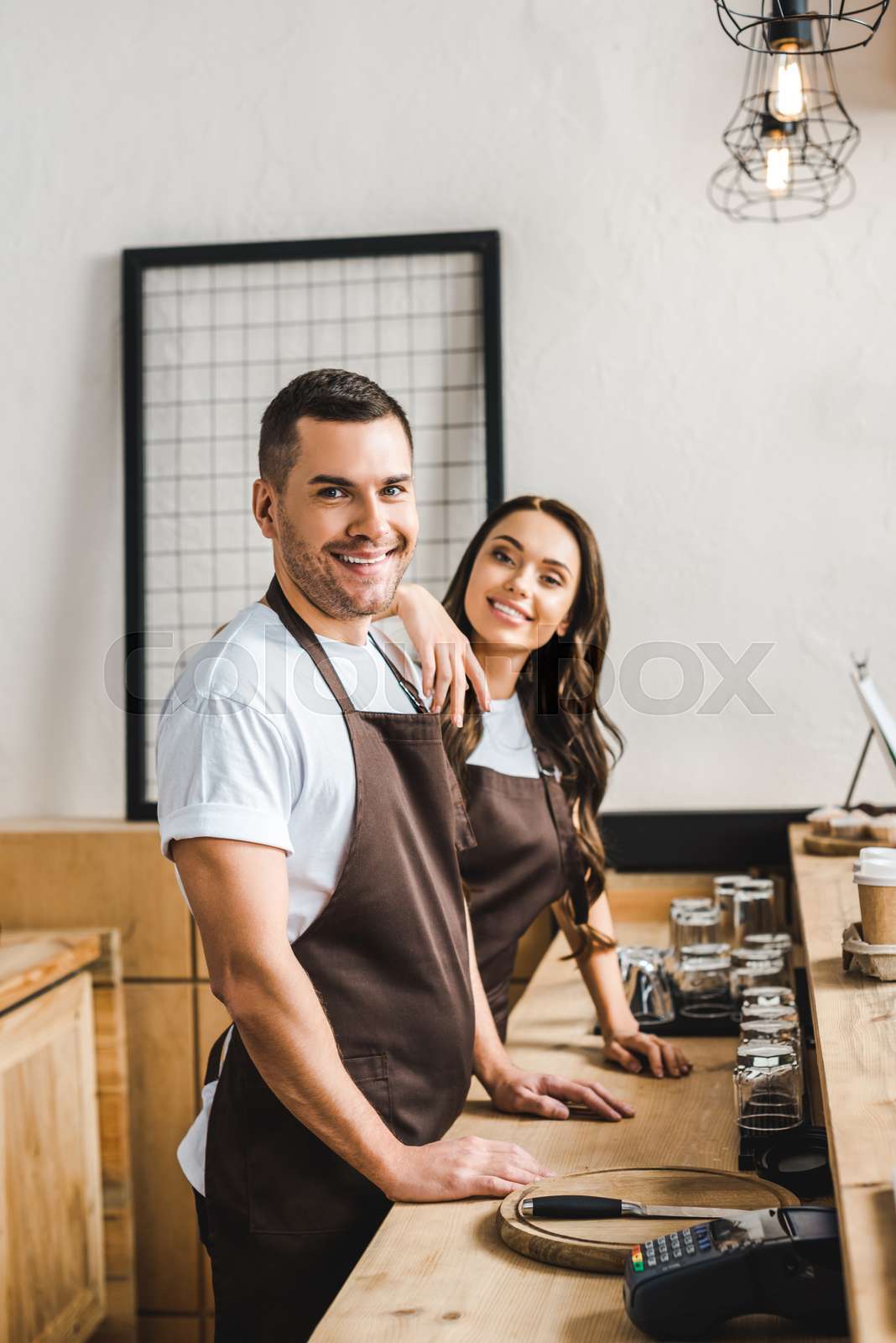 cashiers standing and smiling behind wooden bar counte in coffee house ...