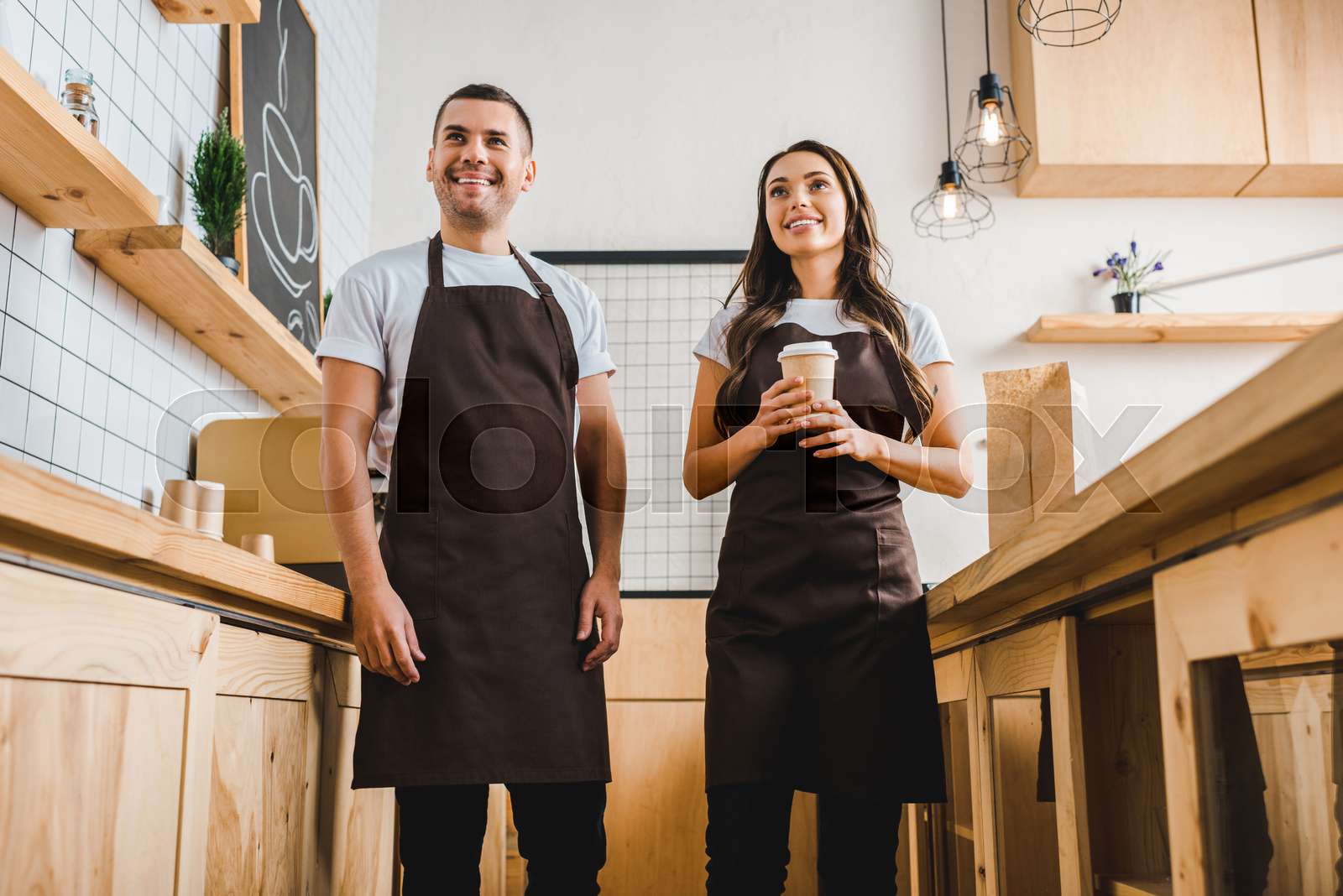 cashiers standing and smiling behind wooden bar counter in coffee house ...
