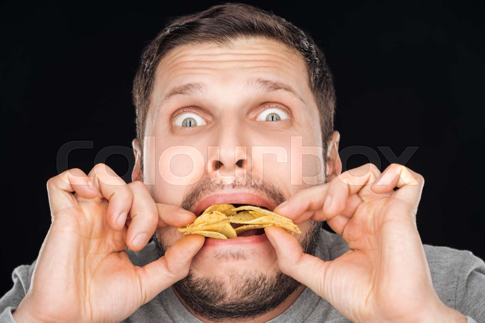 emotionab mal eating chips while looking at camera isolated on black ...