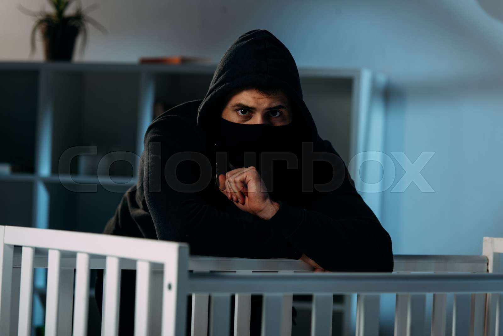 Worried kidnapper in black clothes and mask standing beside crib ...