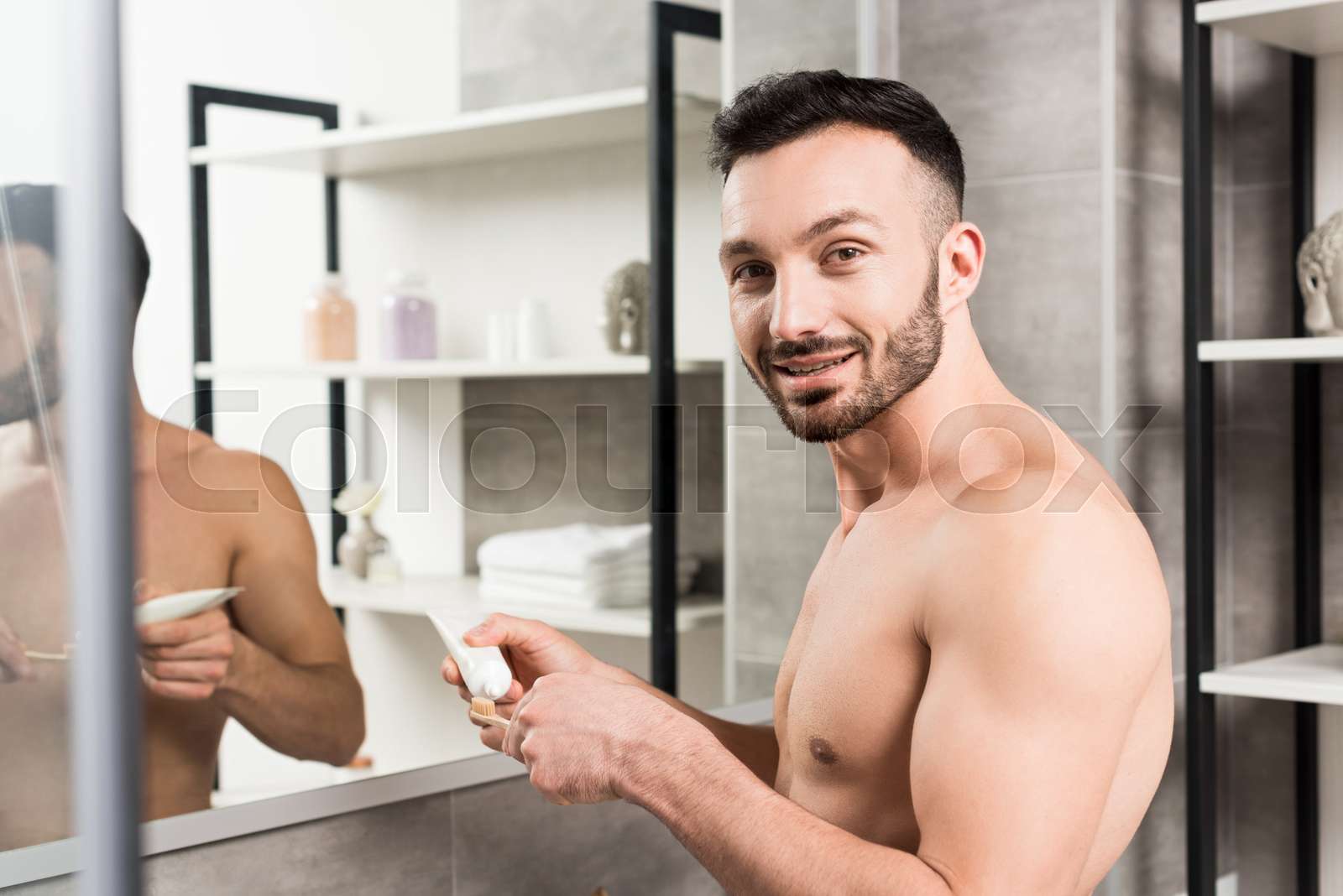 happy shirtless man holding toothpaste and toothbrush in bathroom ...