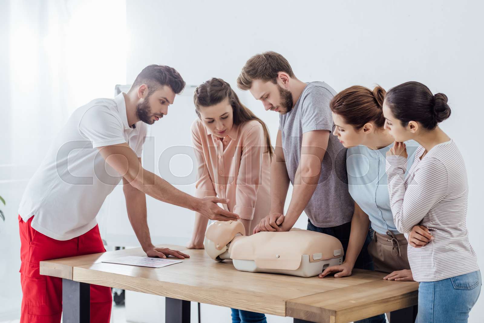 group of people with handsome instructor performing cpr on dummy during ...