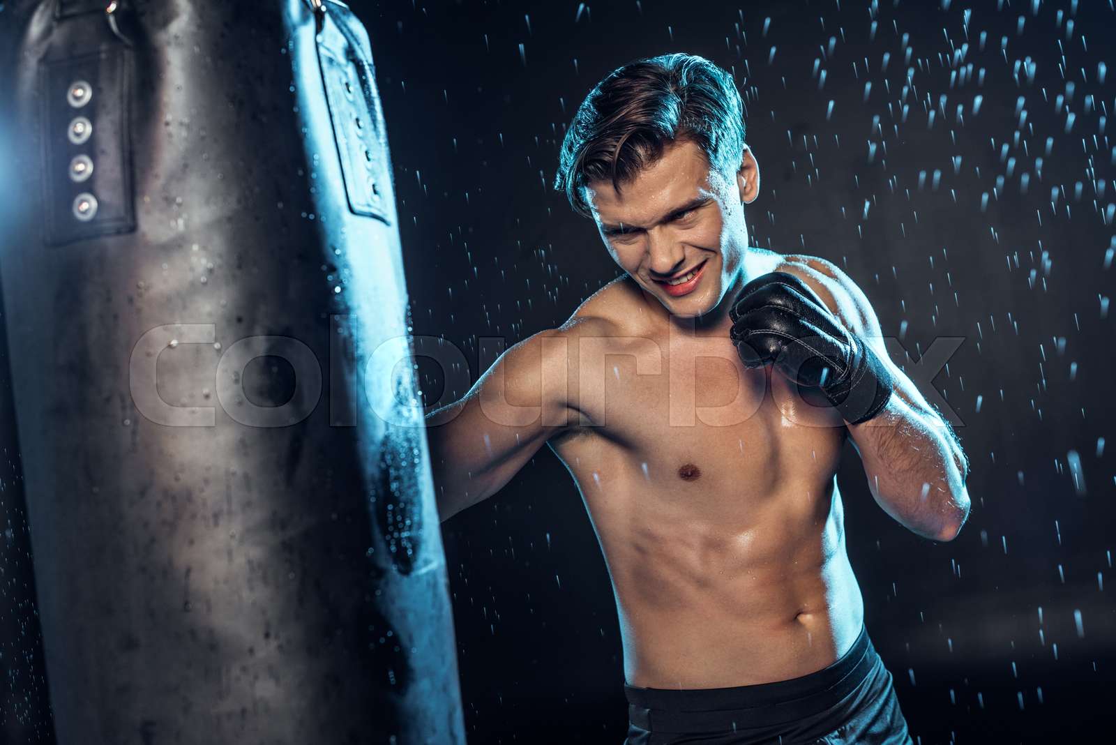Boxer training with punching bag under water drops on black | Stock ...