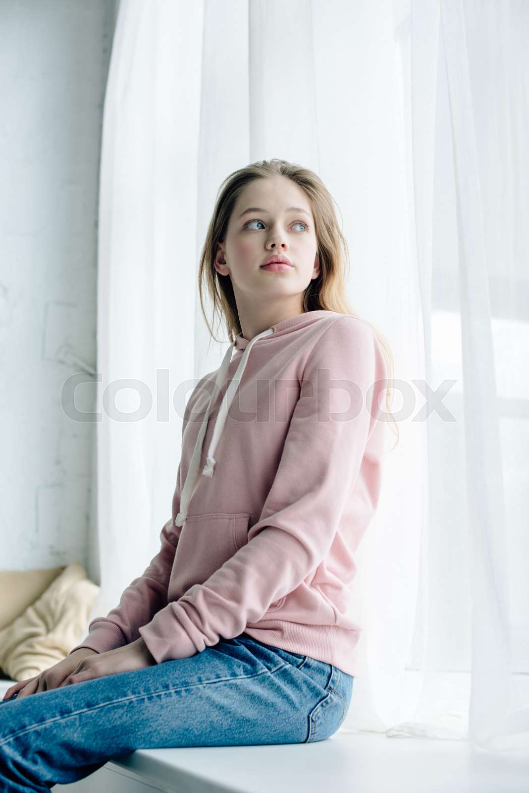 Low angle view of teenager sitting on window sill and looking away ...
