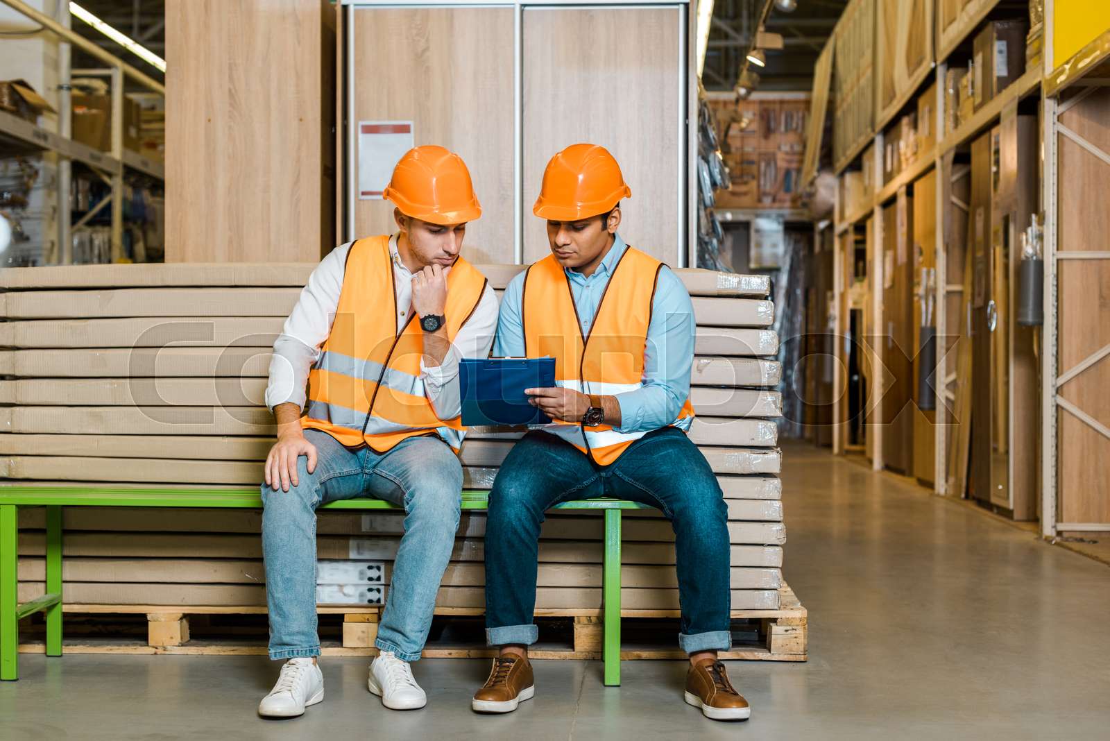 concentrated multicultural workers sitting on bench in warehouse and ...