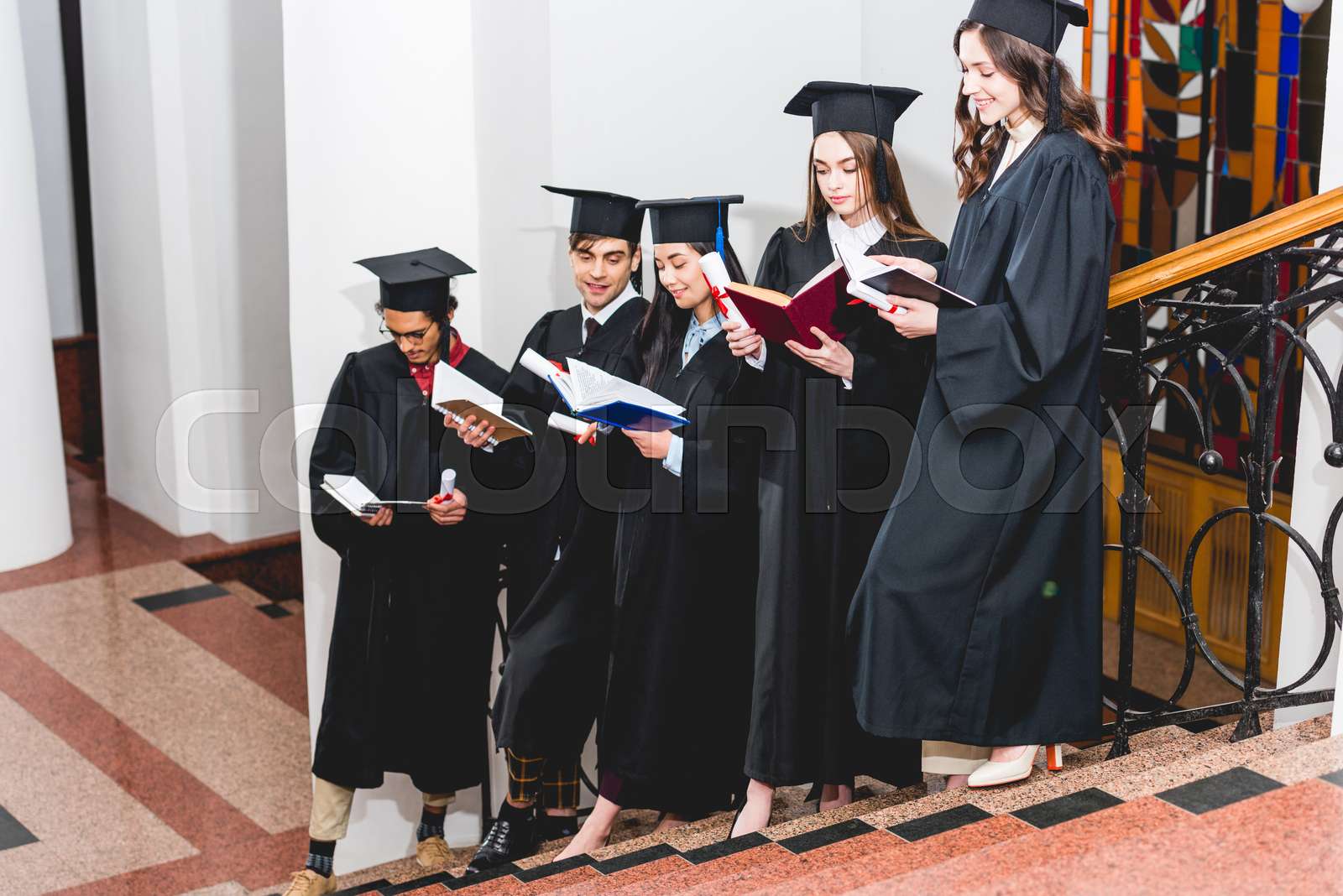 happy students in graduation caps holding diplomas and reading books ...