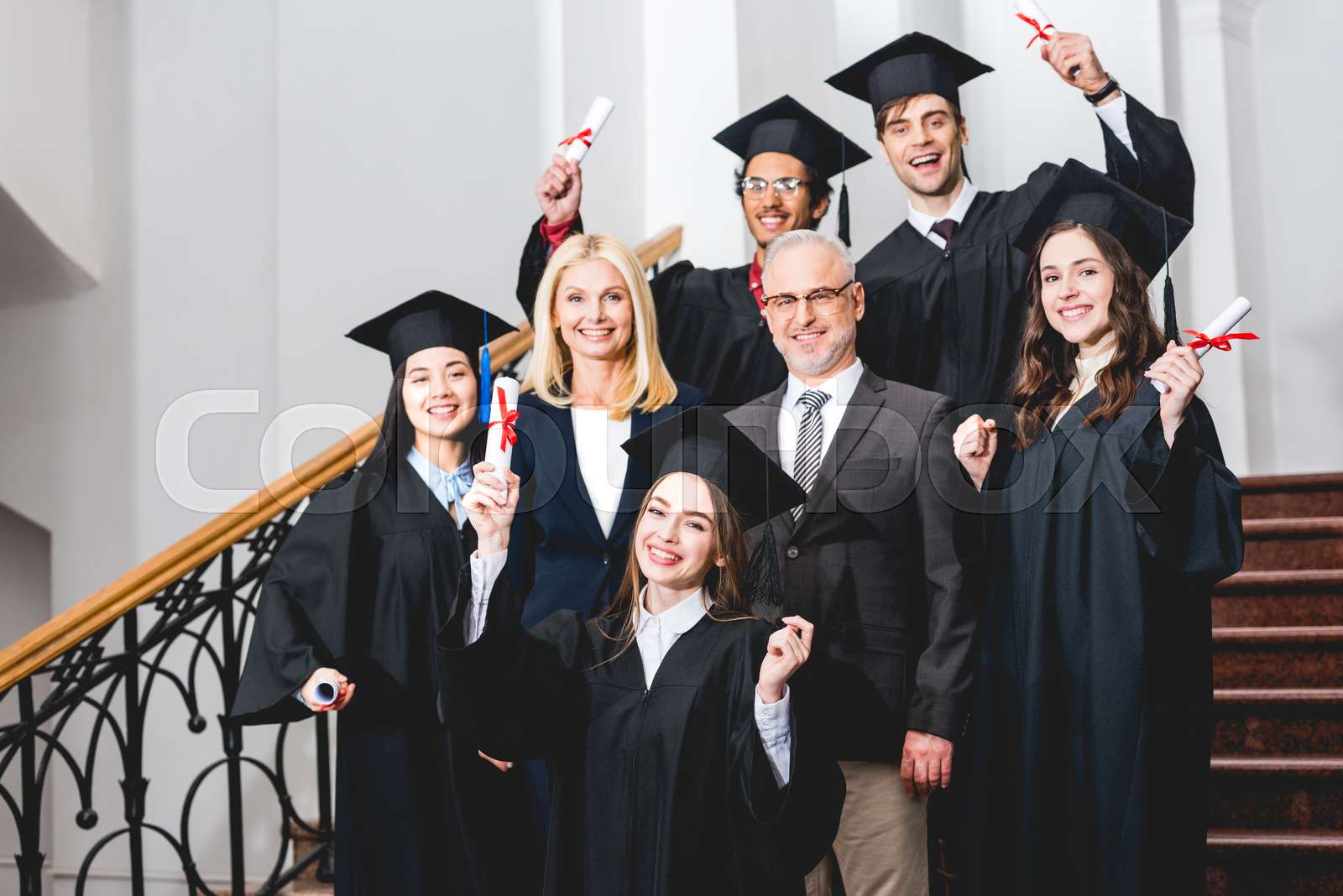 cheerful students in graduation caps holding diplomas near happy ...