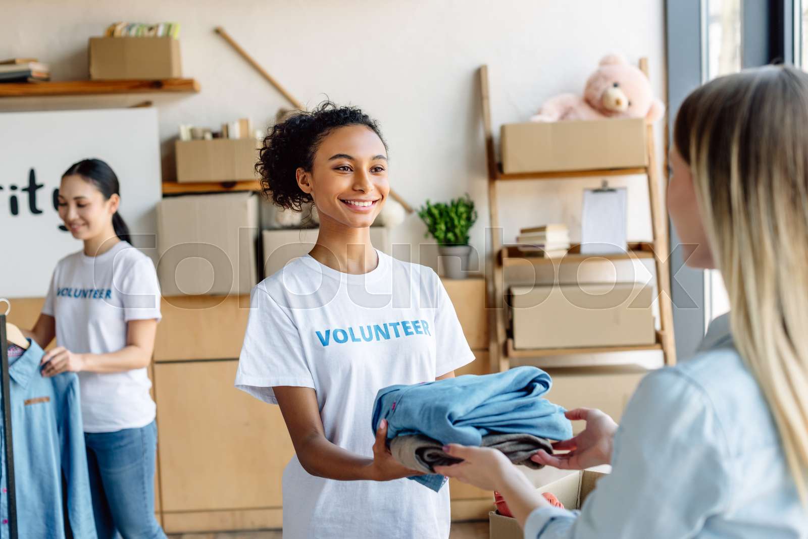 selective focus of smiling african american volunteer giving clothes to ...