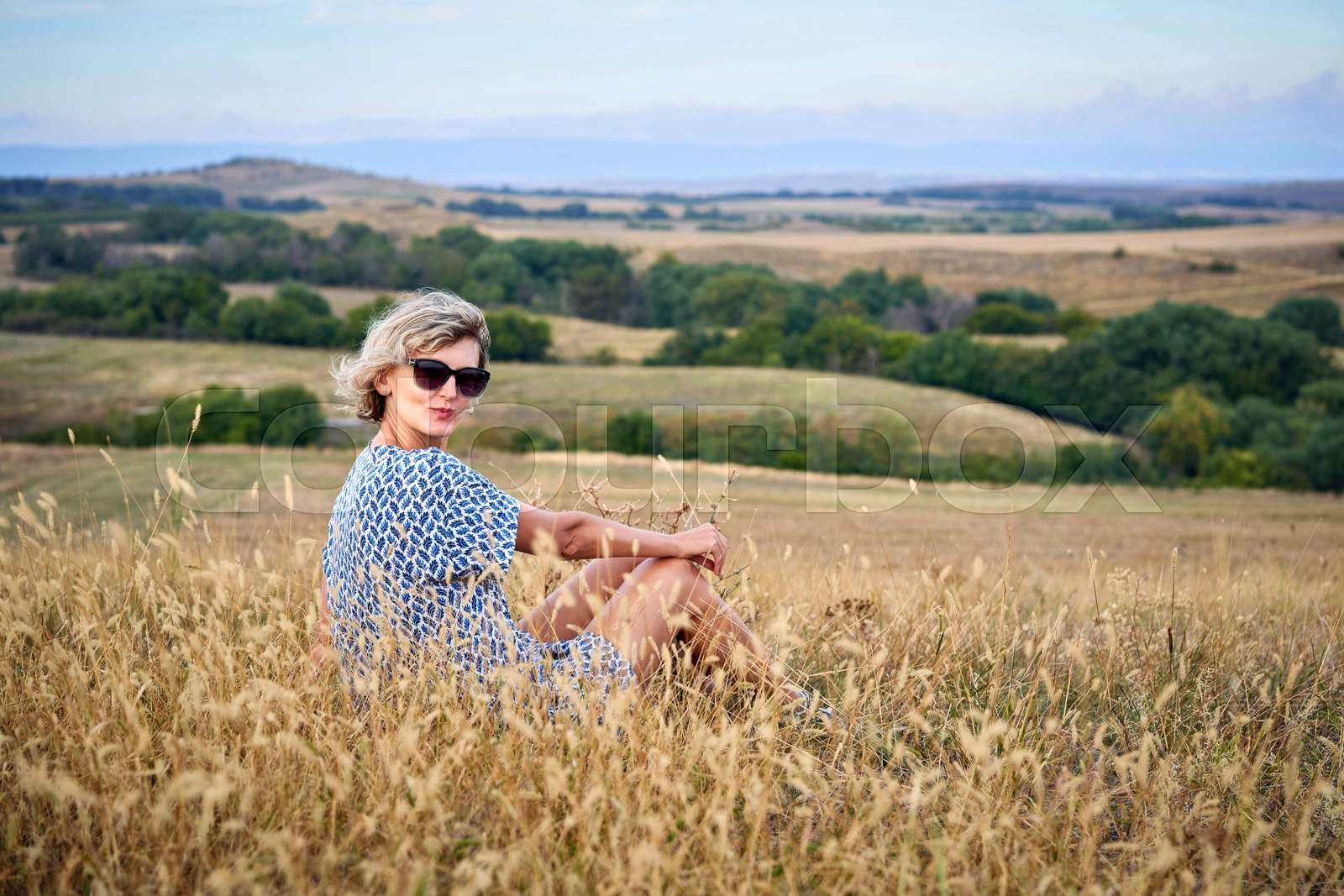 Woman sitting in dry barren grass, looking at camera | Stock image ...
