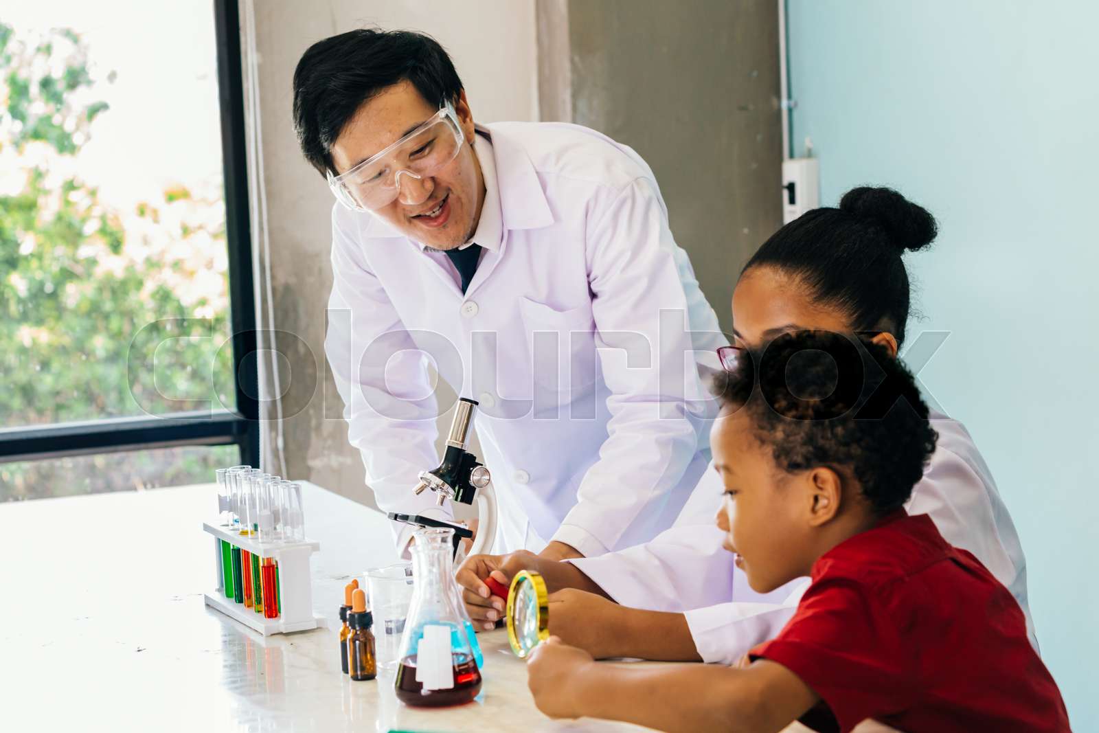Young scientist holding a flask and teaching two African American mixed ...