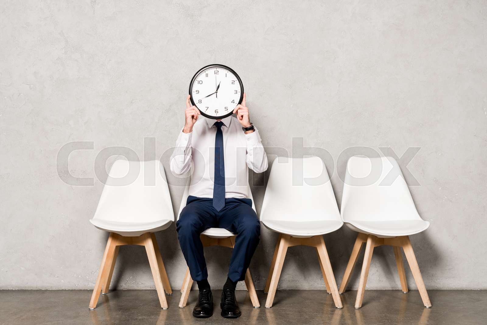 man in formal wear covering face with clock while sitting on chair ...