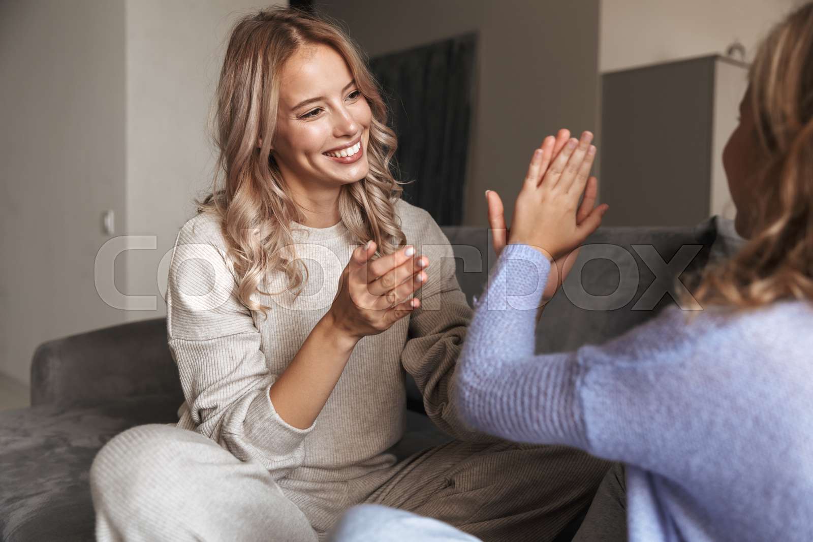 Two scared girls sisters on sofa at home indoors having fun together ...