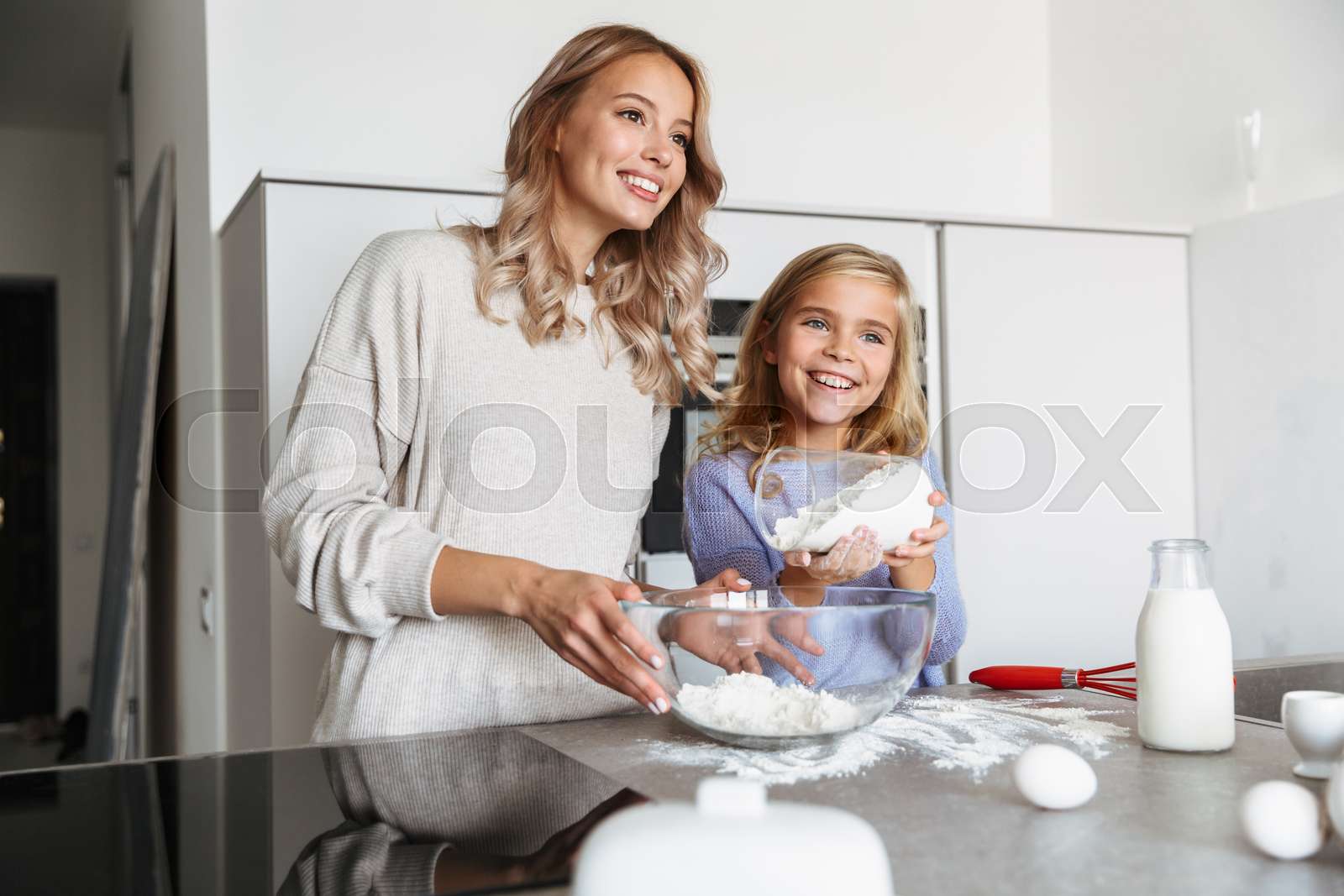 Woman with her little sister indoors at home kitchen cooking with flour ...