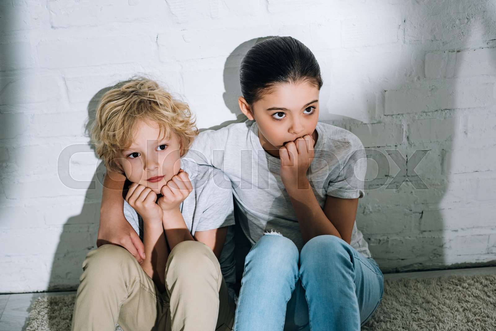 scared sister embracing brother while sitting on carpet | Stock image ...