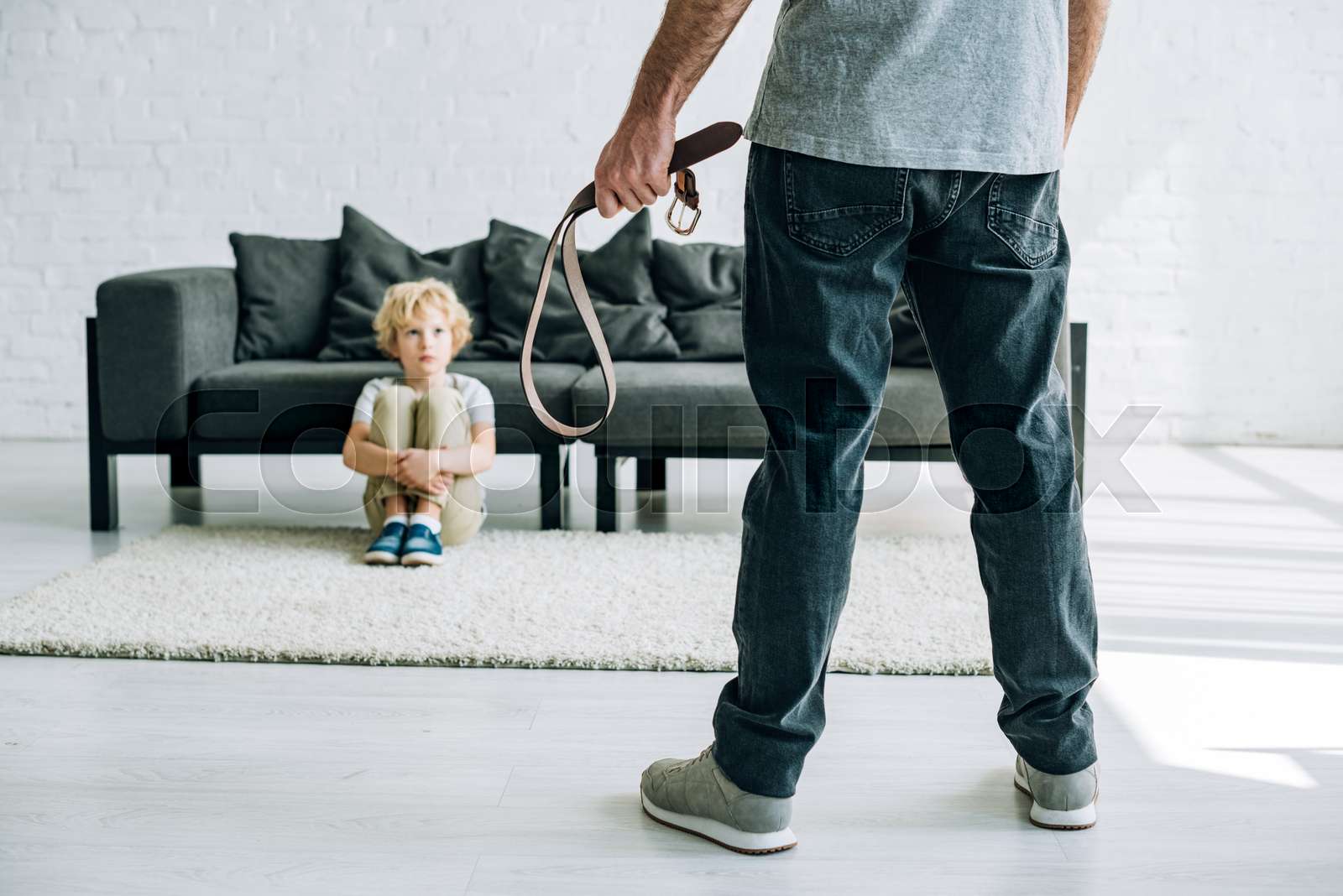 partial view of abusive father holding belt and sad son sitting on ...