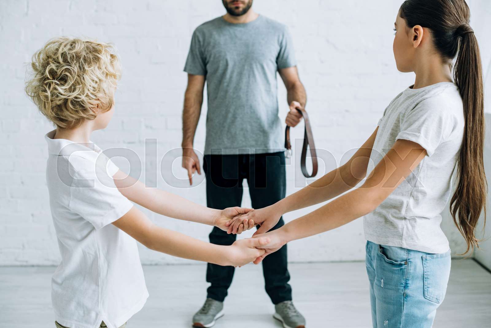 partial view of abusive father with belt and kids holding hands | Stock ...