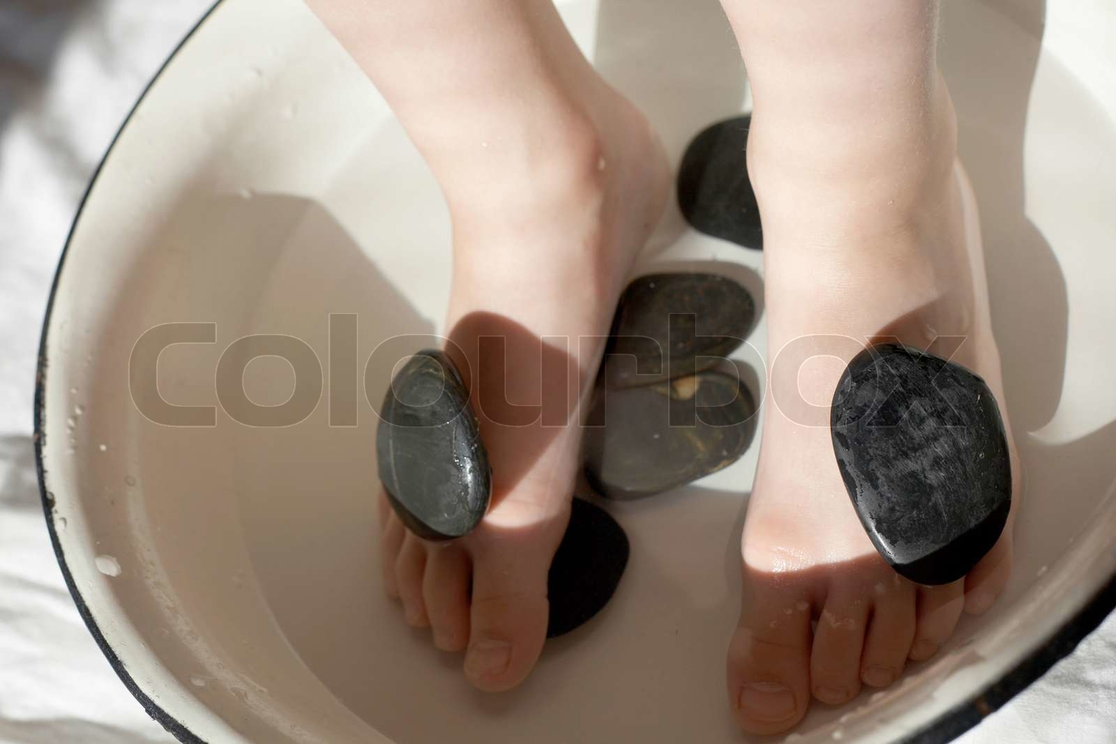 Child's feet in wash-basin with stones | Stock image | Colourbox