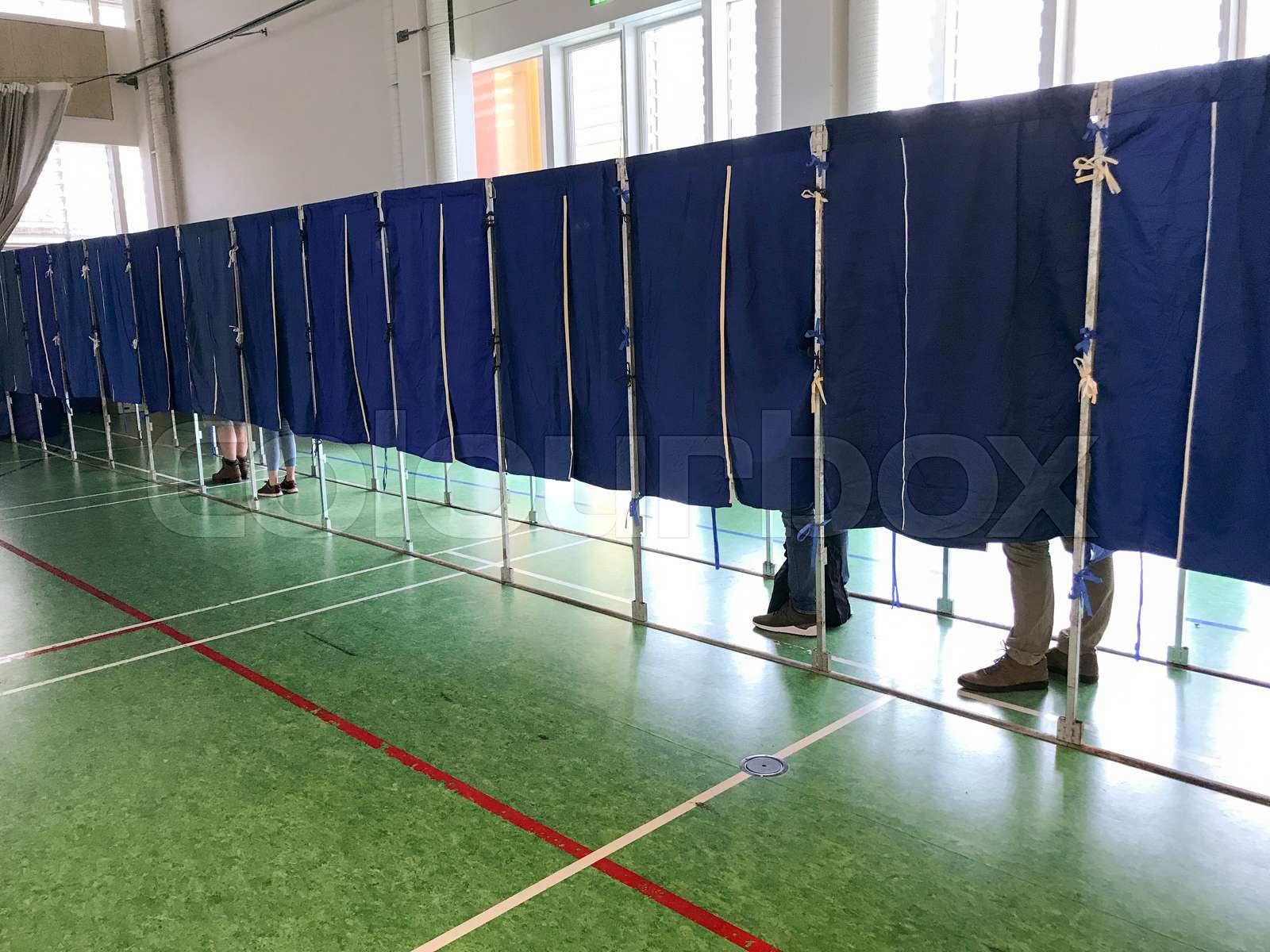 People voting in polling booths at a voting station at a school gym ...