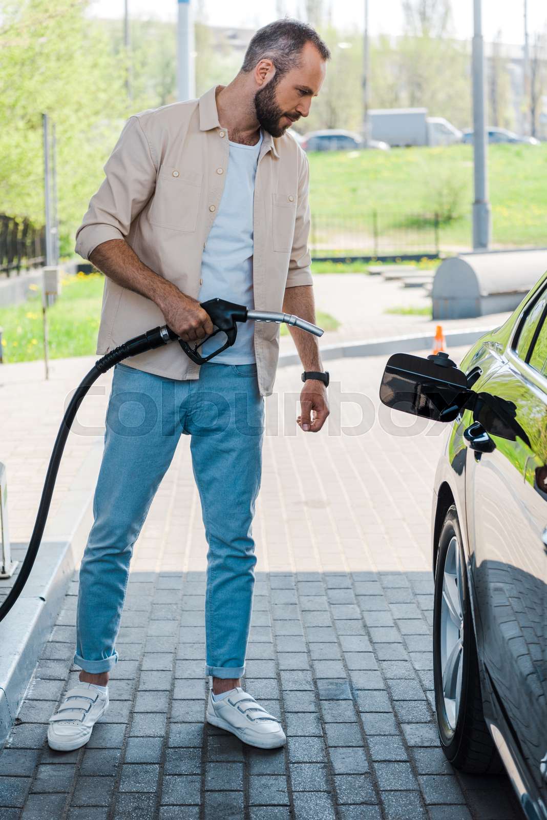 handsome man holding fuel nozzle near black car at gas station | Stock ...