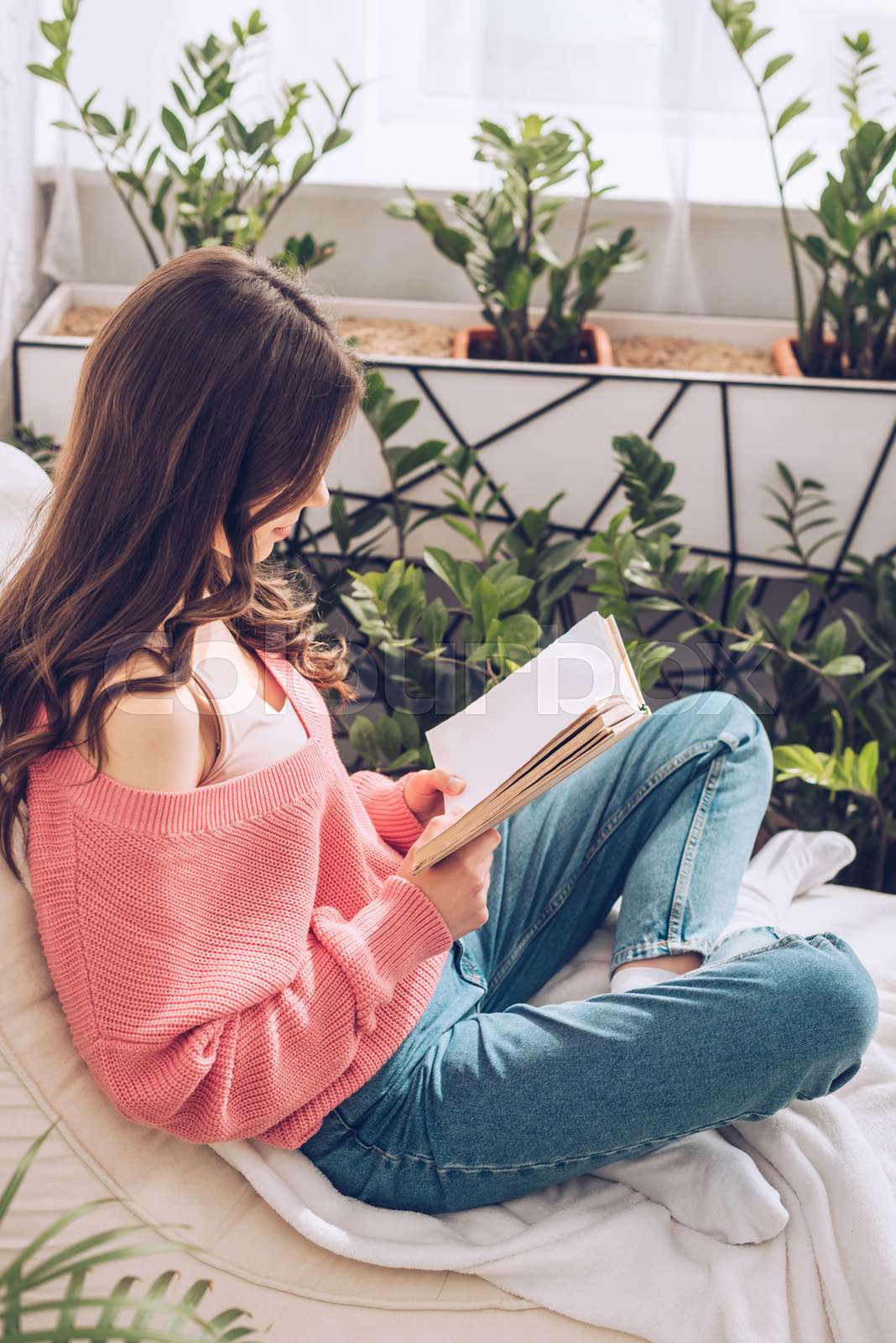 young woman reading book while sitting surrounded by green plants at ...