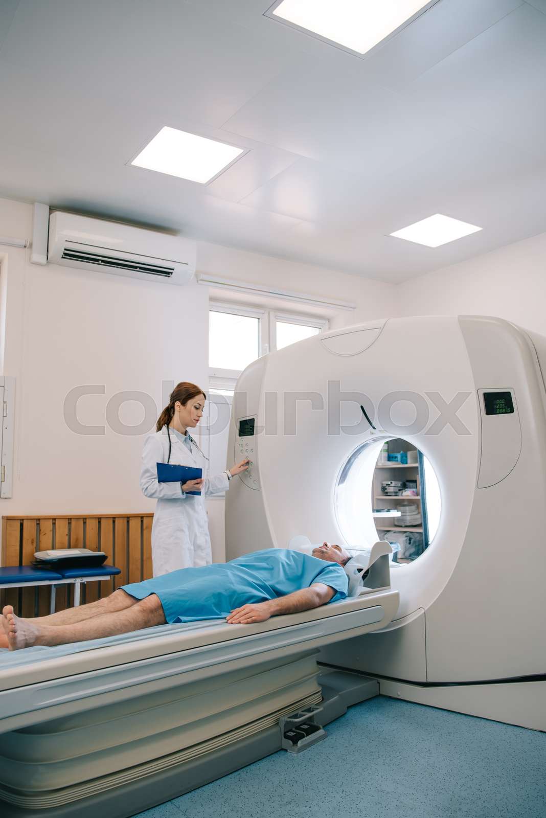 radiologist in white coat operating ct scanner while patient lying on ...