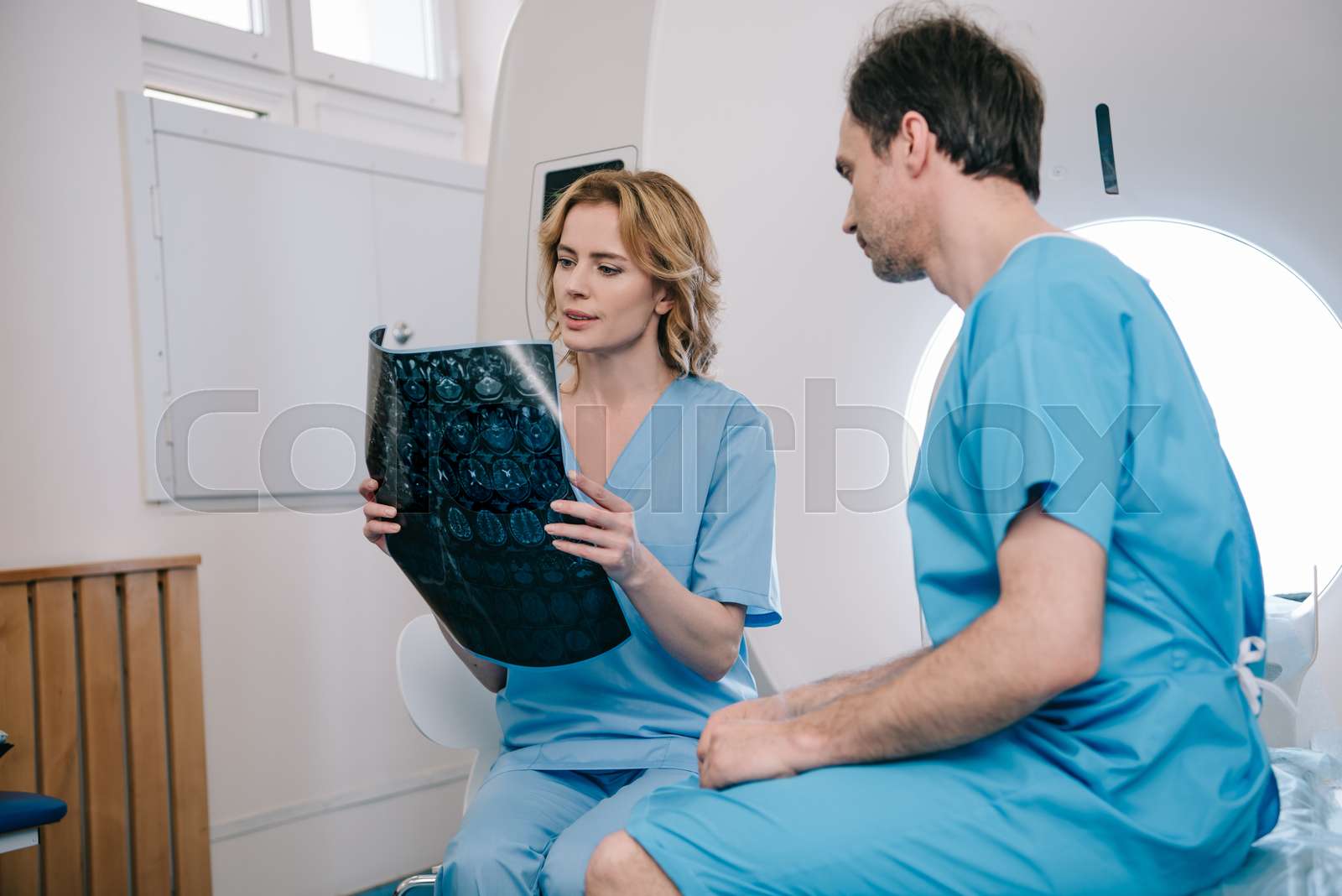 attentive radiographer looking at x-ray diagnosis near patient sitting ...