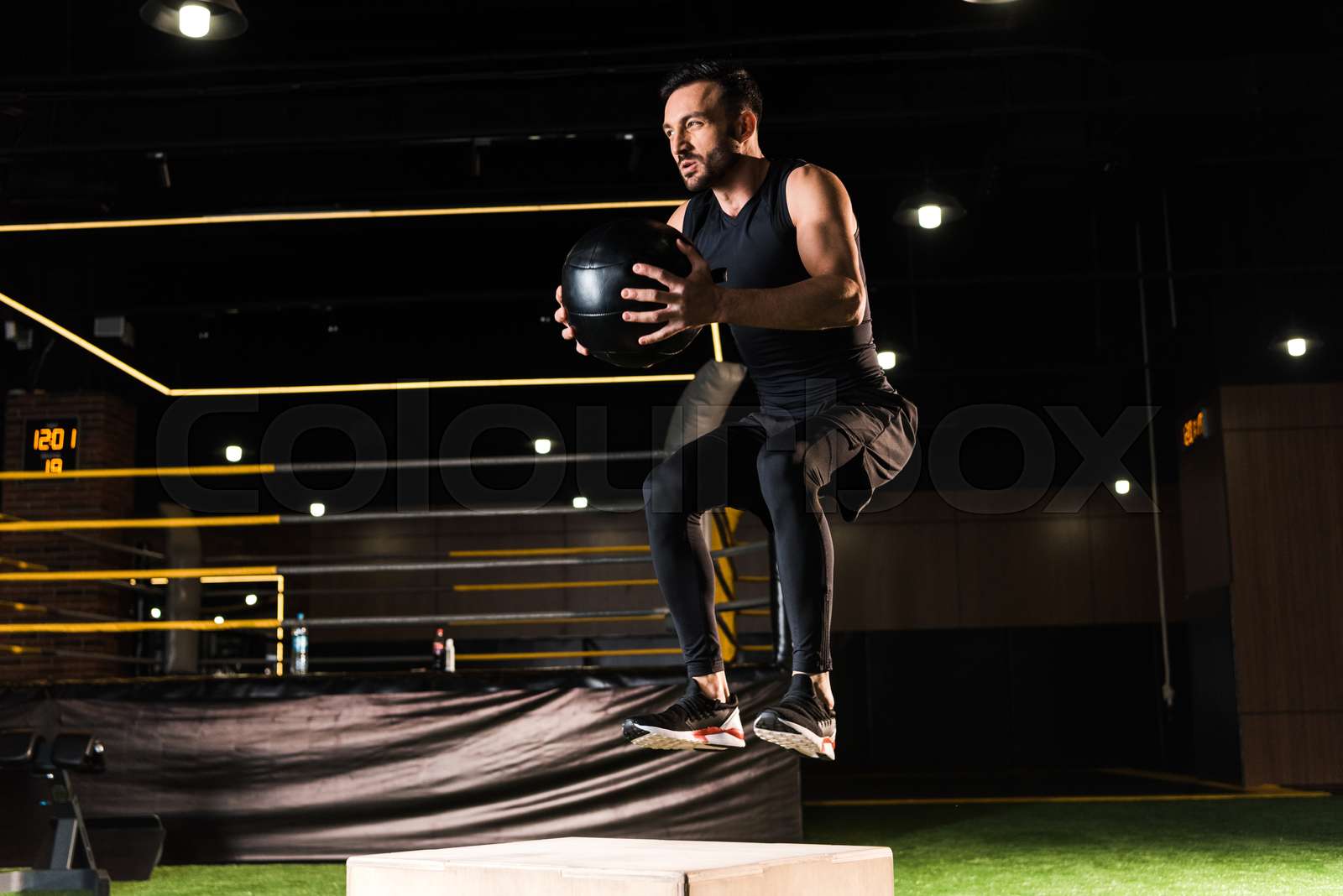 low angle view of serious man jumping on squat box while holding ball ...