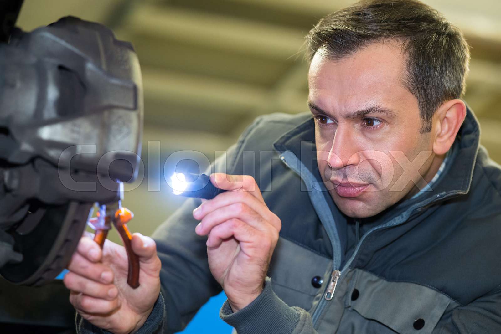 mechanic examining a car with torch at the repair garage | Stock image ...