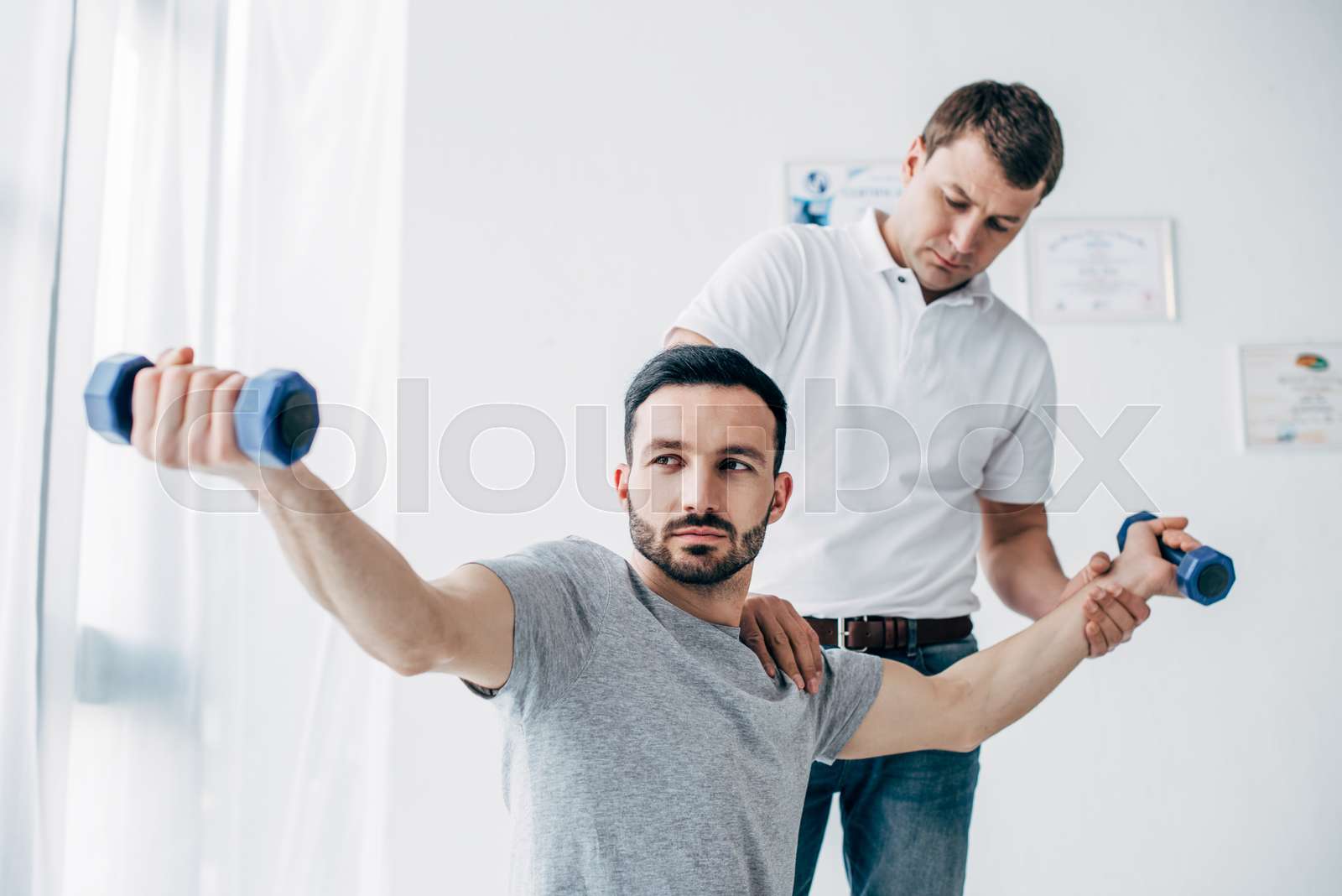 chiropractor stretching arm of handsome patient with dumbbells in ...