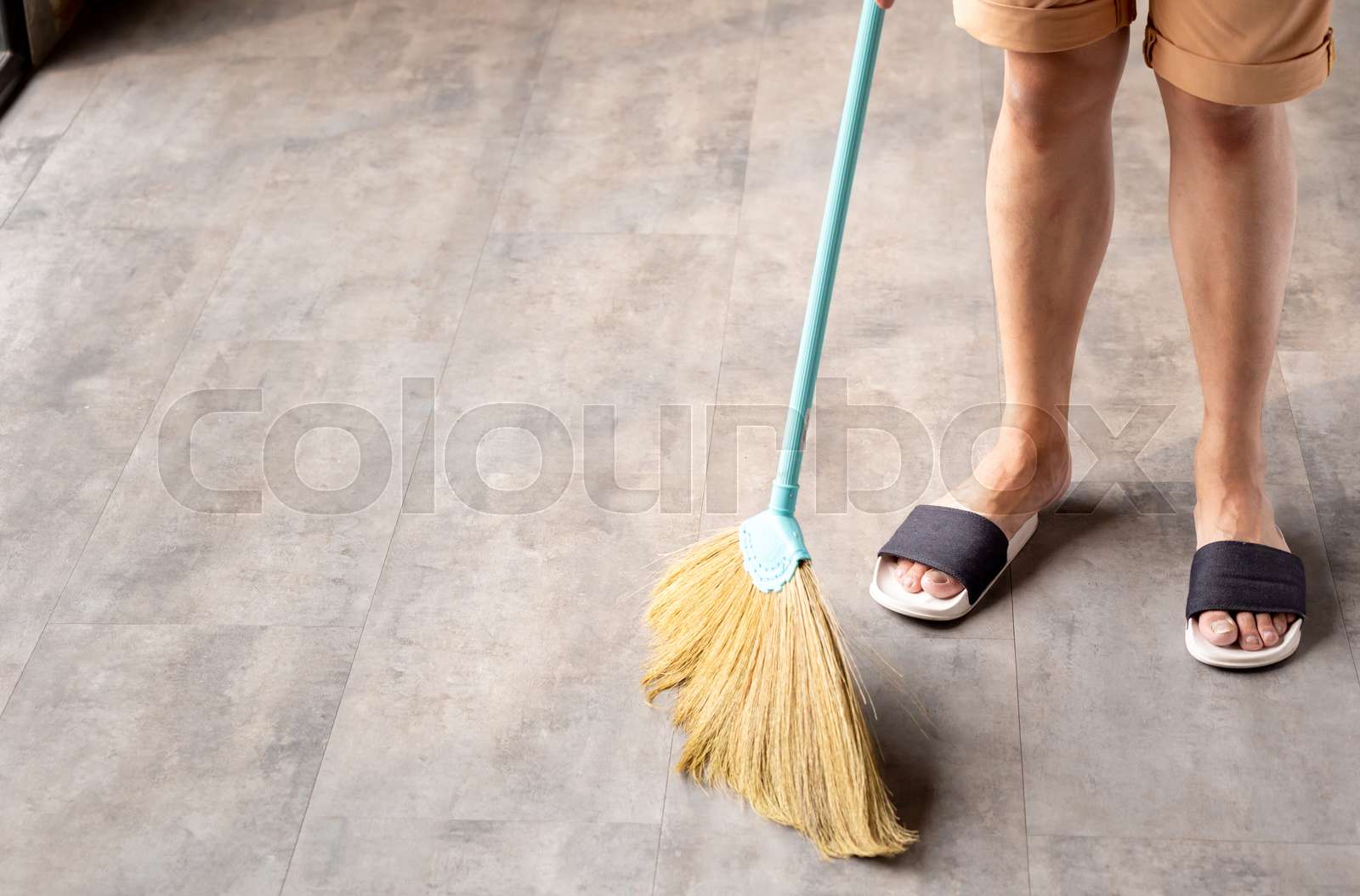 Human legs wearing slippters using sweeping broom inside the house ...