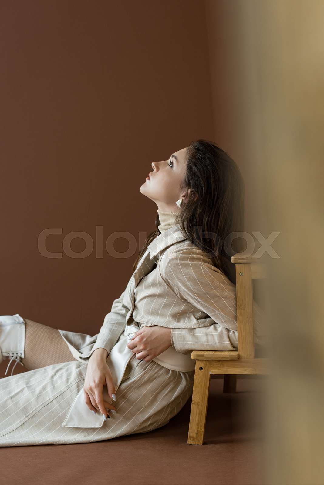 side view of beautiful and trendy woman sitting on floor, looking up ...