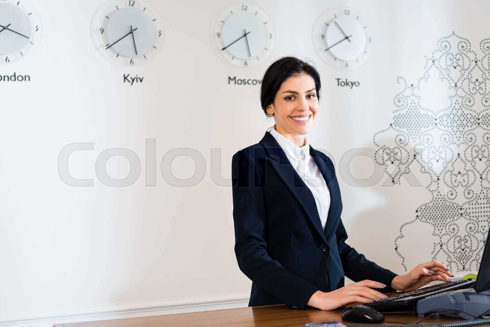 attractive receptionist smiling while standing at reception desk ...