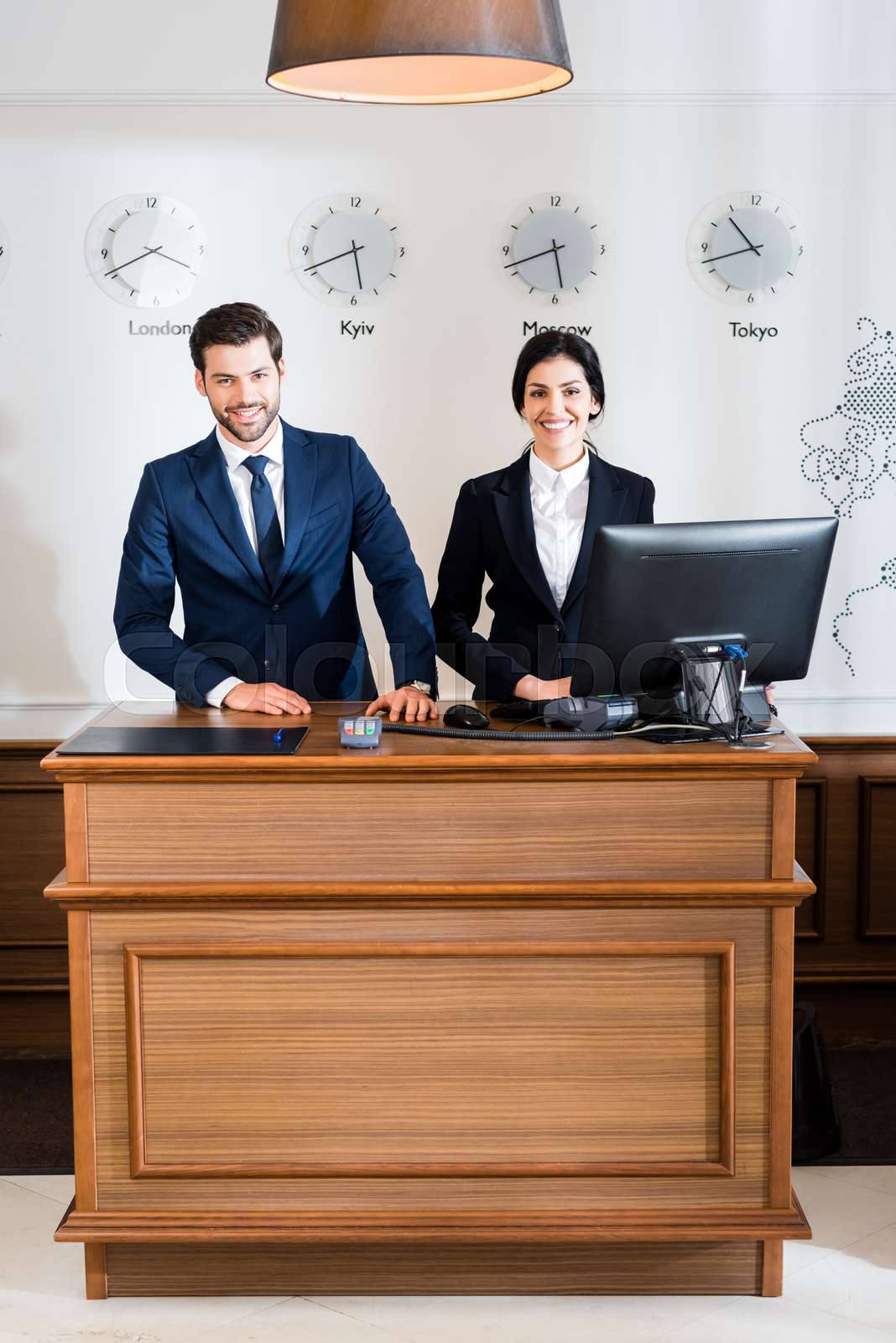 cheerful receptionists in formal wear standing at reception desk ...