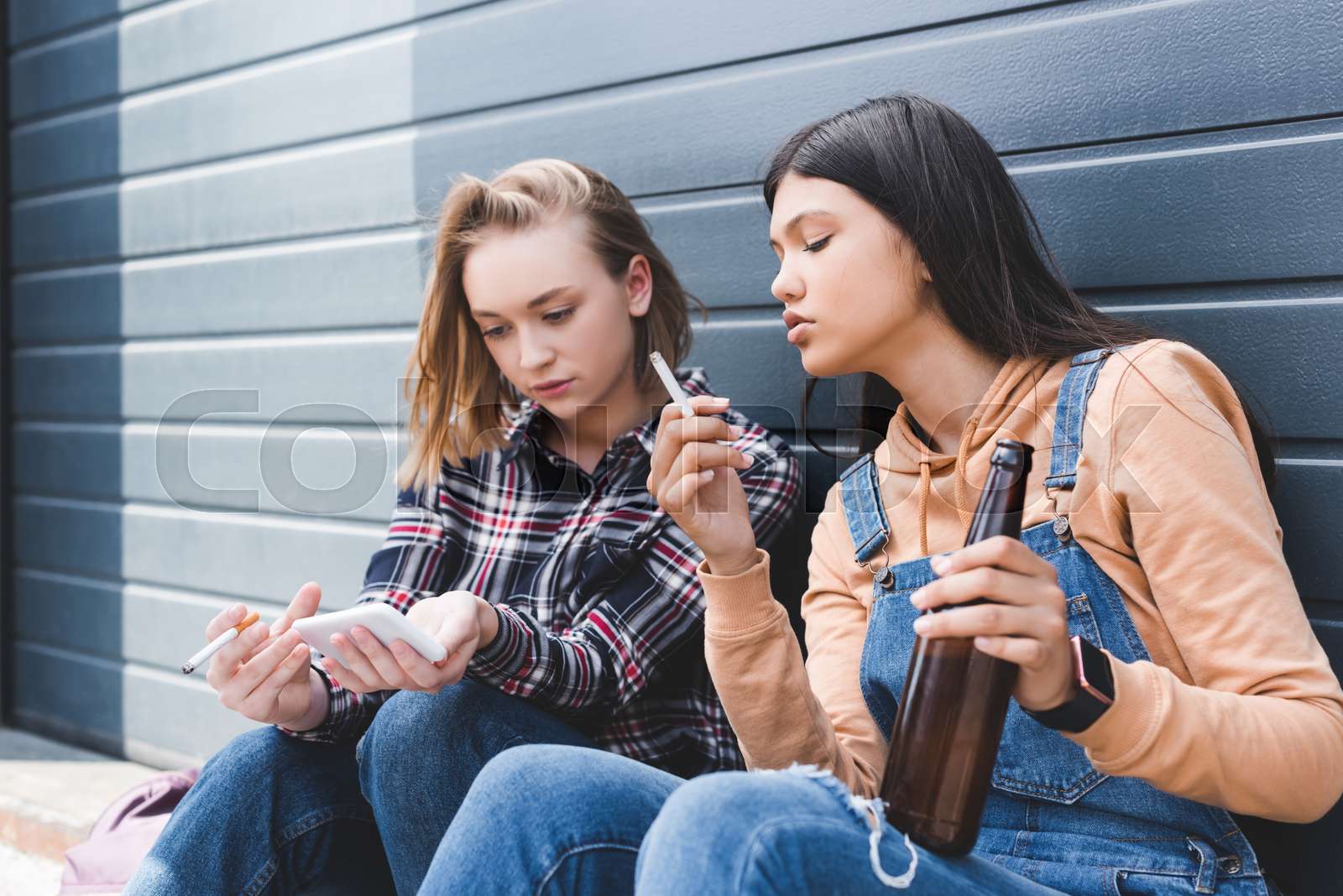 pretty friends smoking cigarettes, holding beer, sitting and looking at ...