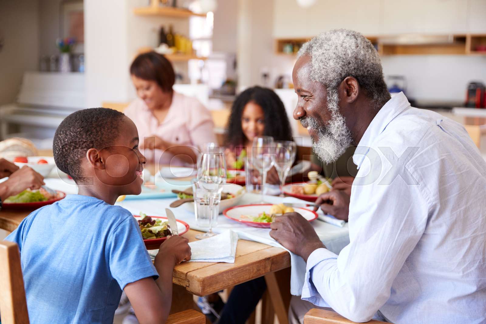 Multi-Generation Family Sitting Around Table At Home Enjoying Meal ...