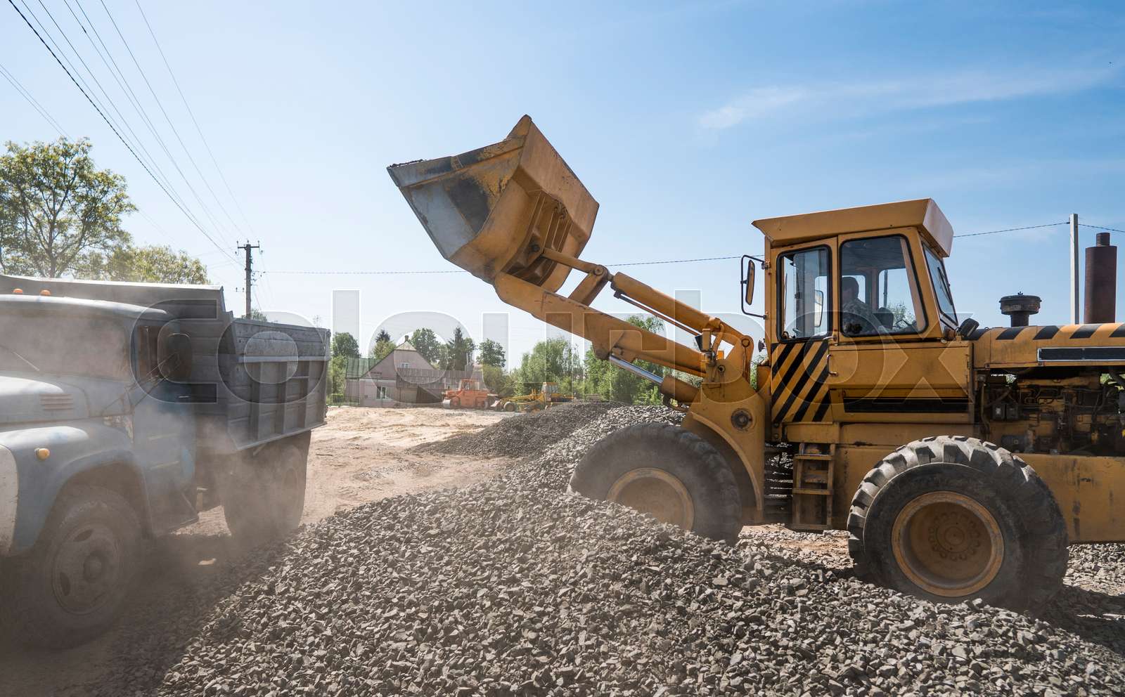 Yellow loader delivering stone gravel into truck during road ...