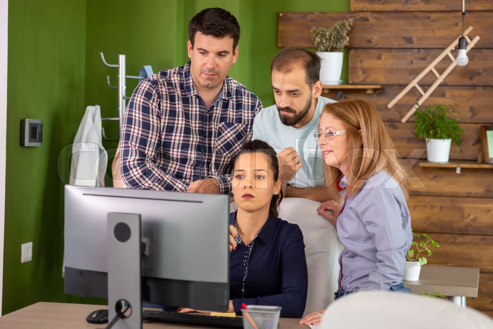 Team gathered behind their manager looking into computer monitor ...
