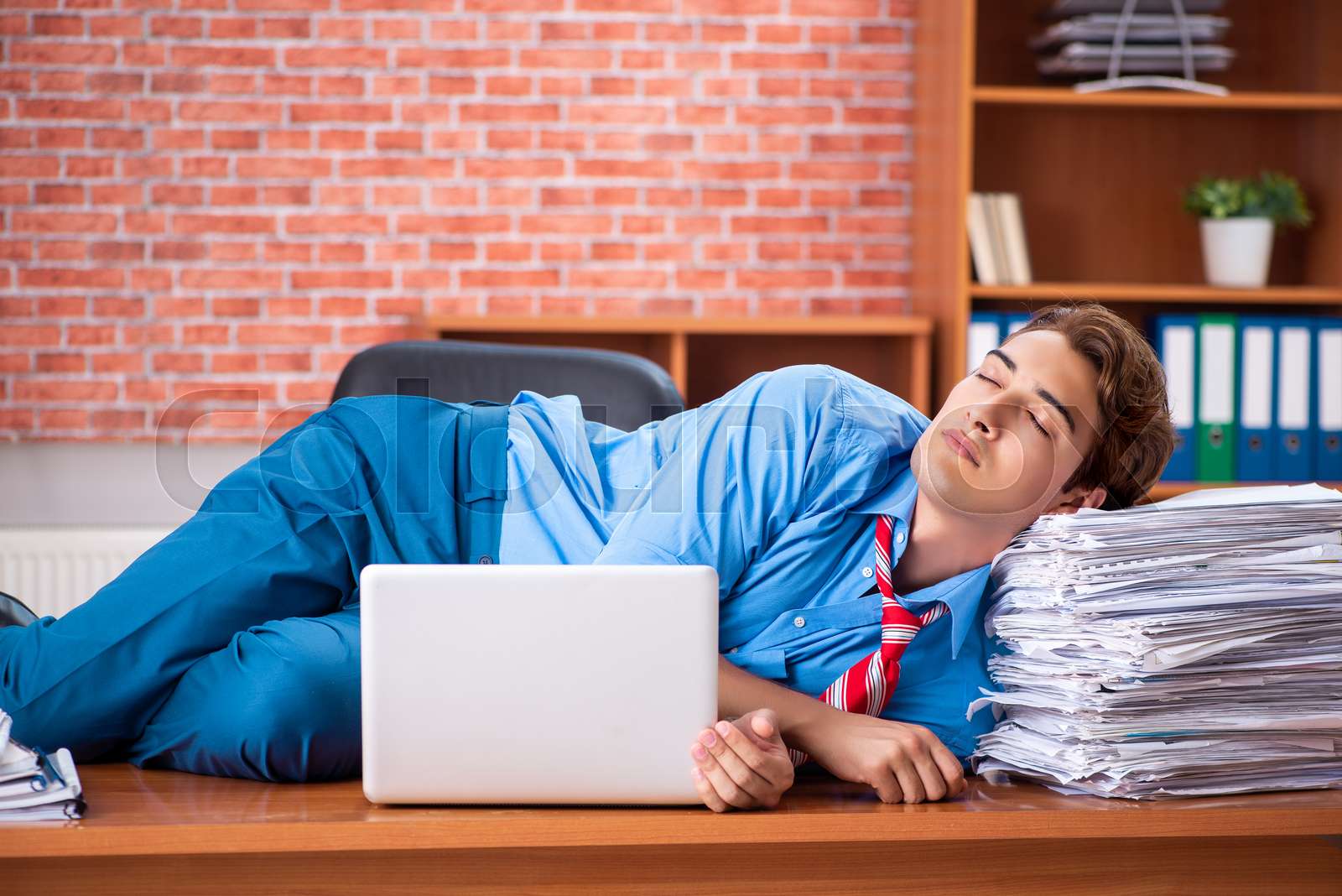 The young employee with excessive work sitting at the office | Stock ...