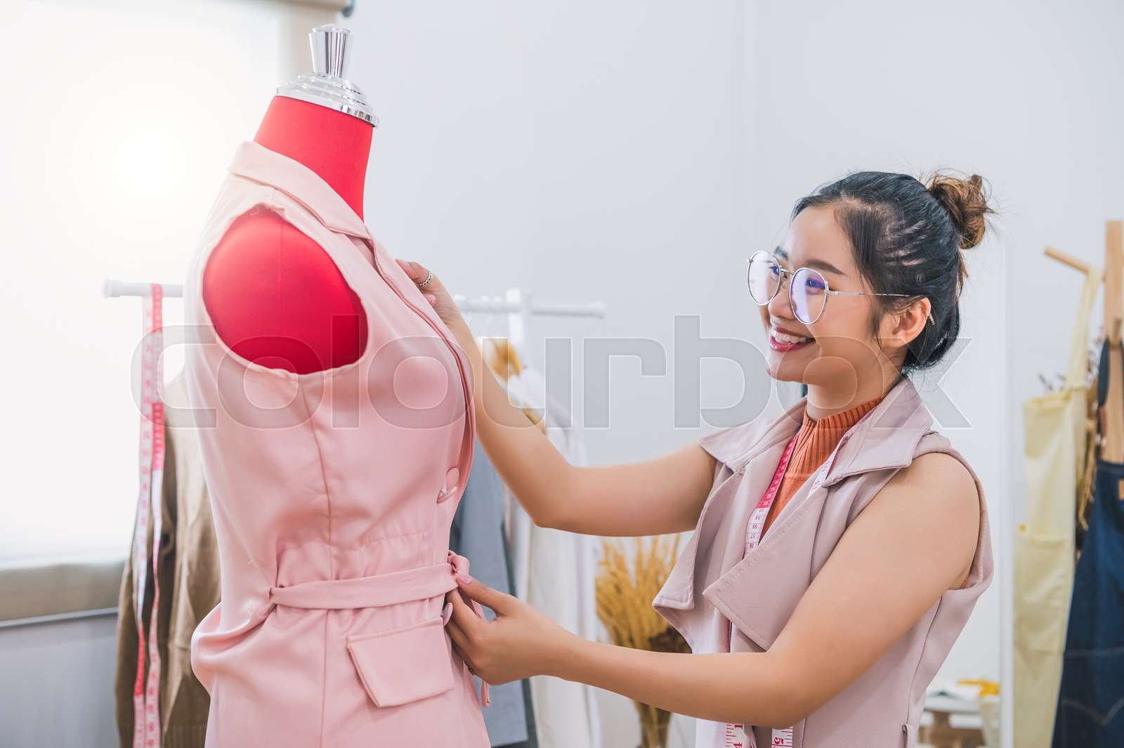 Happy Asian female fashion designer girl making fit on the formal dress ...