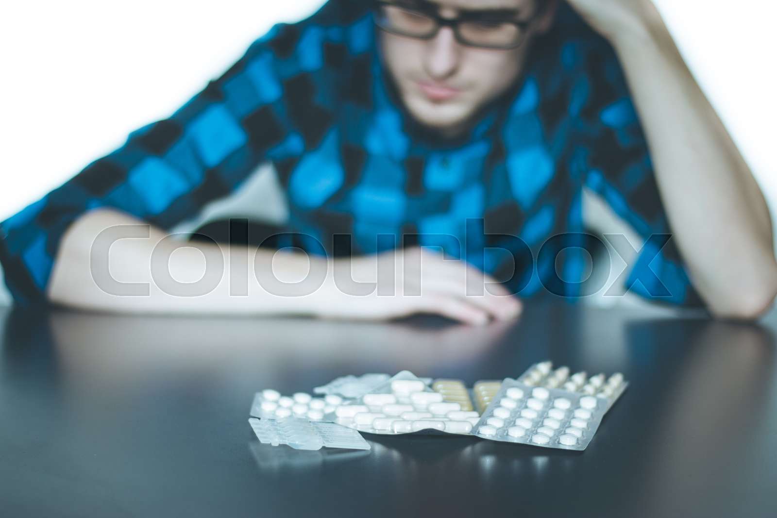 Depressed man taking drugs. Young man sitting on a table, drugs and ...