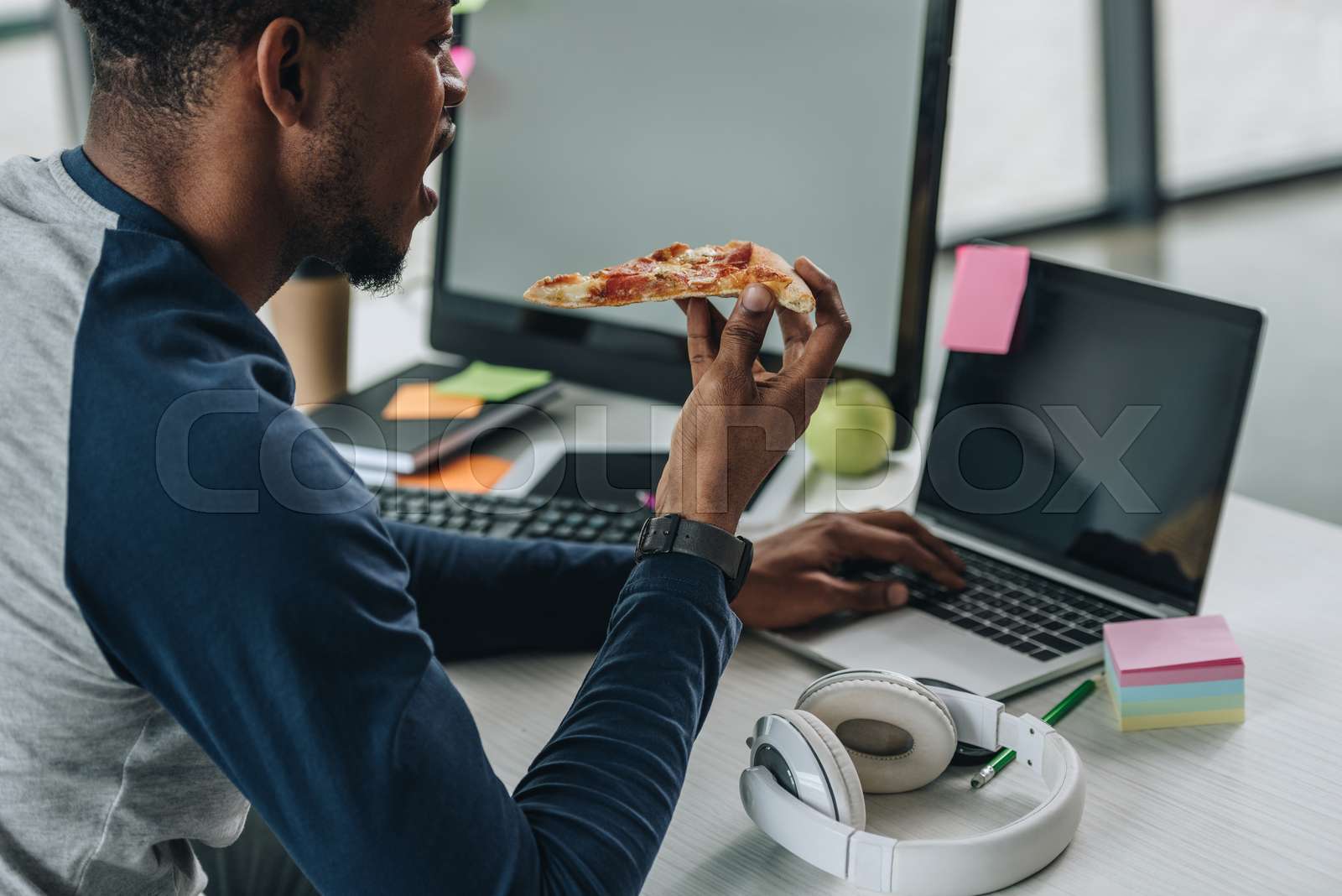 african american programmer eating pizza while working on laptop | Stock image | Colourbox