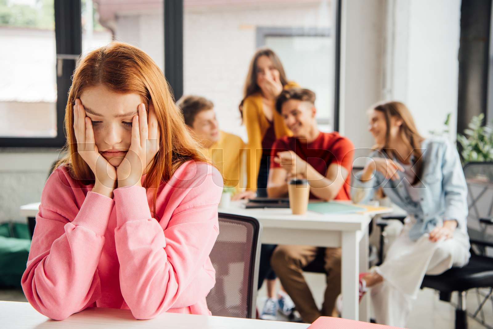 sad girl sitting in front of laughing classmates | Stock image | Colourbox