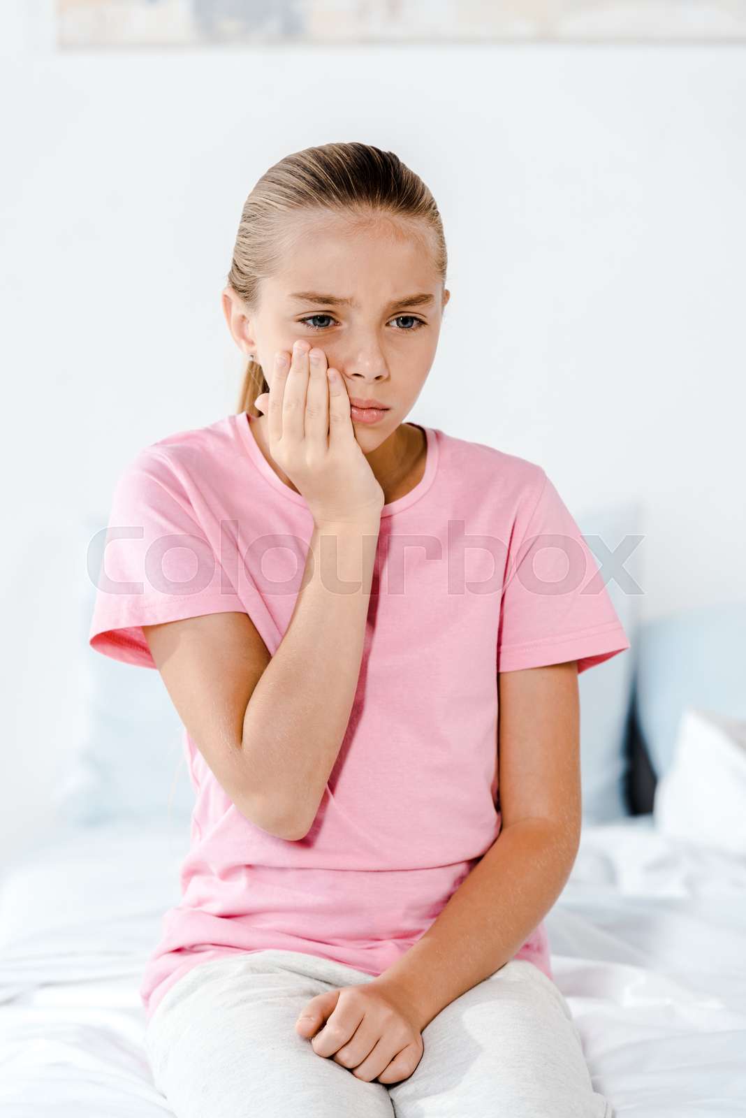 upset kid touching cheek while having tooth ache | Stock image | Colourbox