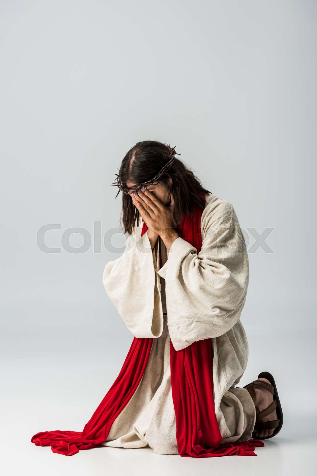 jesus in wreath covering face while praying on knees on grey | Stock ...