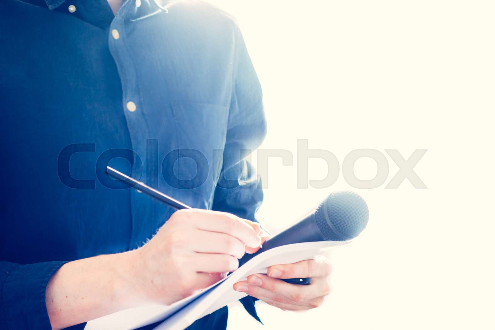 Male journalist at news conference, holding microphone and taking notes ...